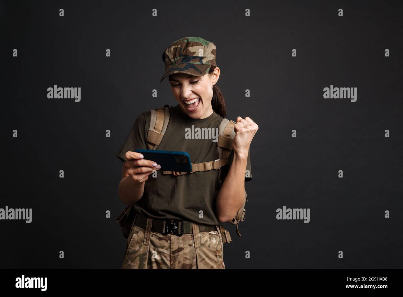 Excited soldier woman making winner gesture while using mobile phone ...