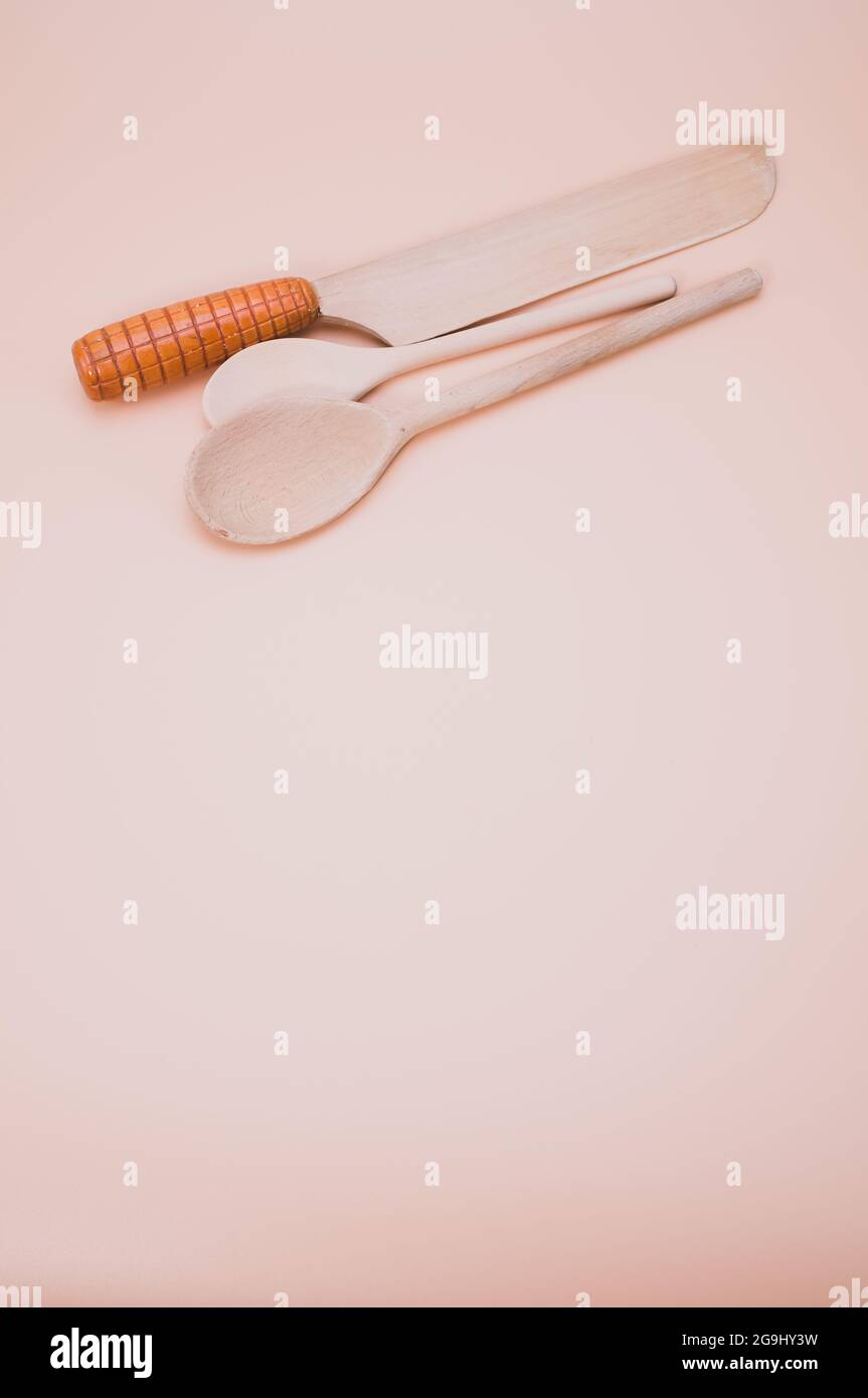 Vertical closeup of wooden spoons and a knife on an aesthetic peach ...