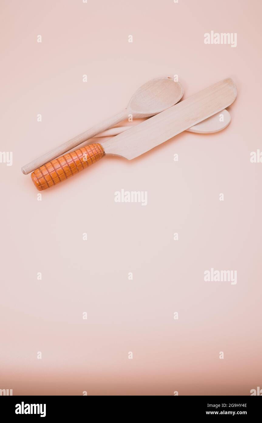 Vertical closeup of wooden spoons and a knife on an aesthetic peach ...