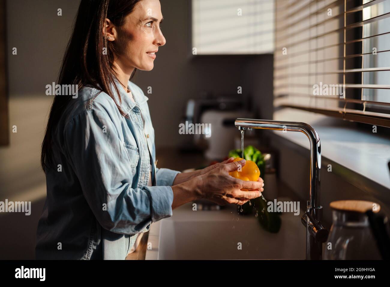 Smiling young woman washing vegetable in the sink in kitchen Stock ...