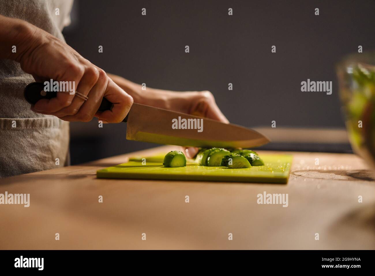 Caucasian woman wearing apron cutting cucumber at home kitchen Stock ...