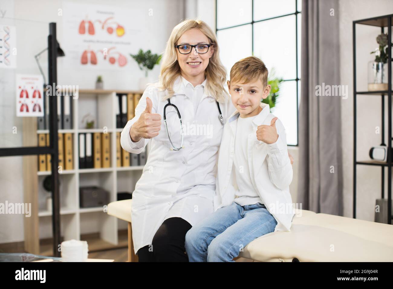 Pretty cheerful female doctor hugging her little child boy patient and ...
