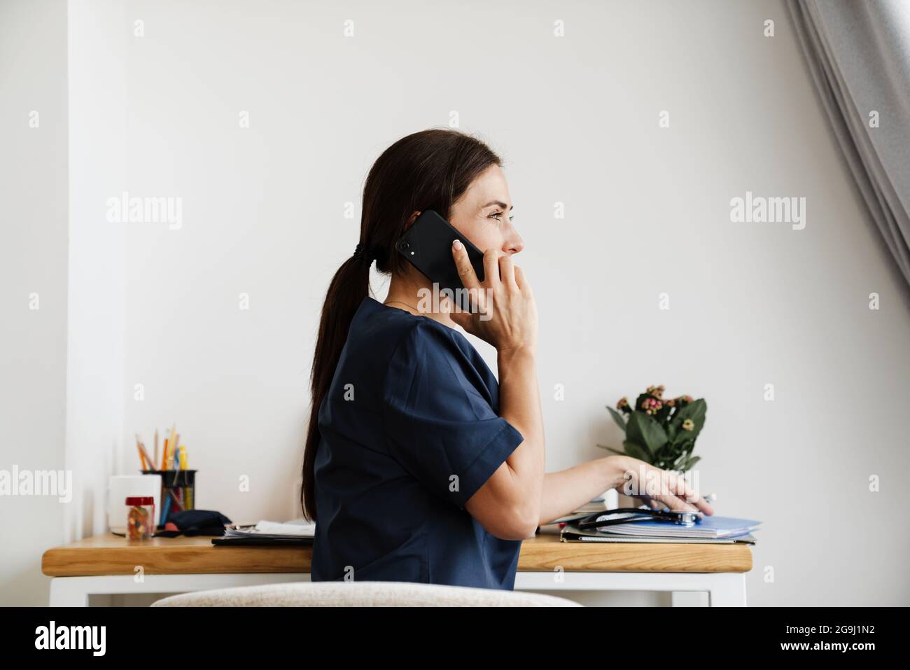 The side view of woman doctor sitting on chair at table and talking on ...