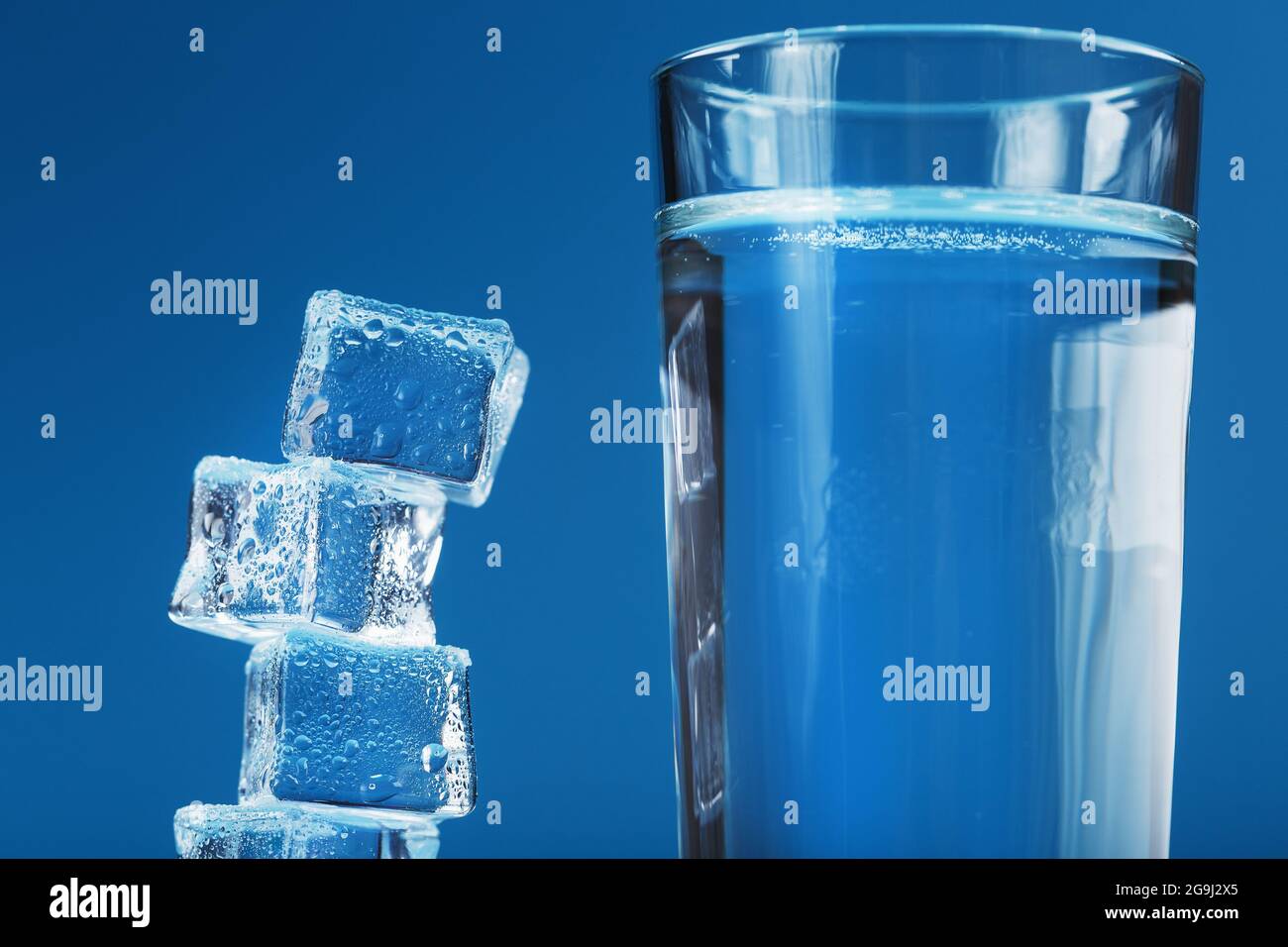 Ice cubes tower with a glass of cold and clean water on a blue ...