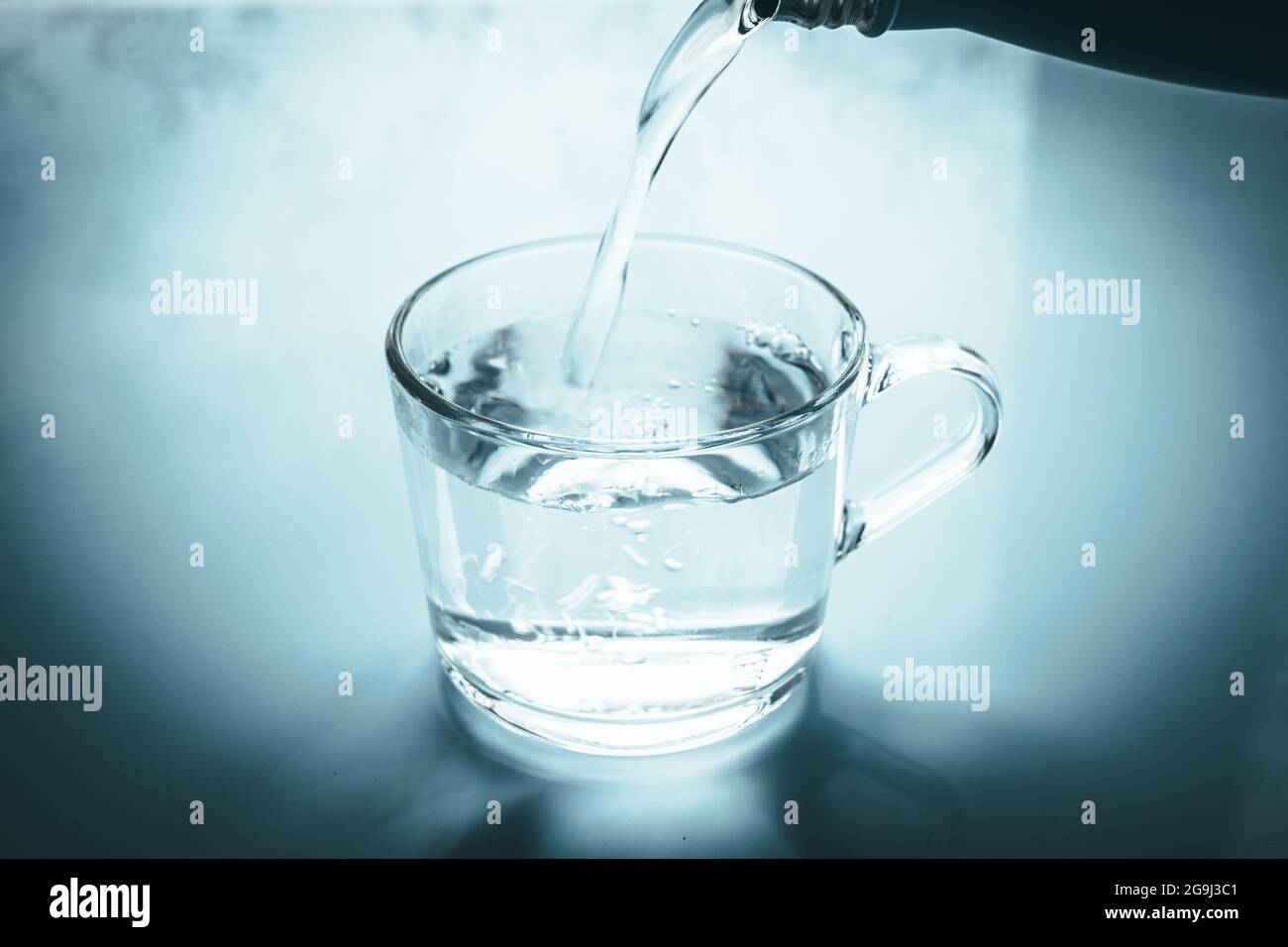 Pouring water into a glass, blue pastel background Stock Photo - Alamy