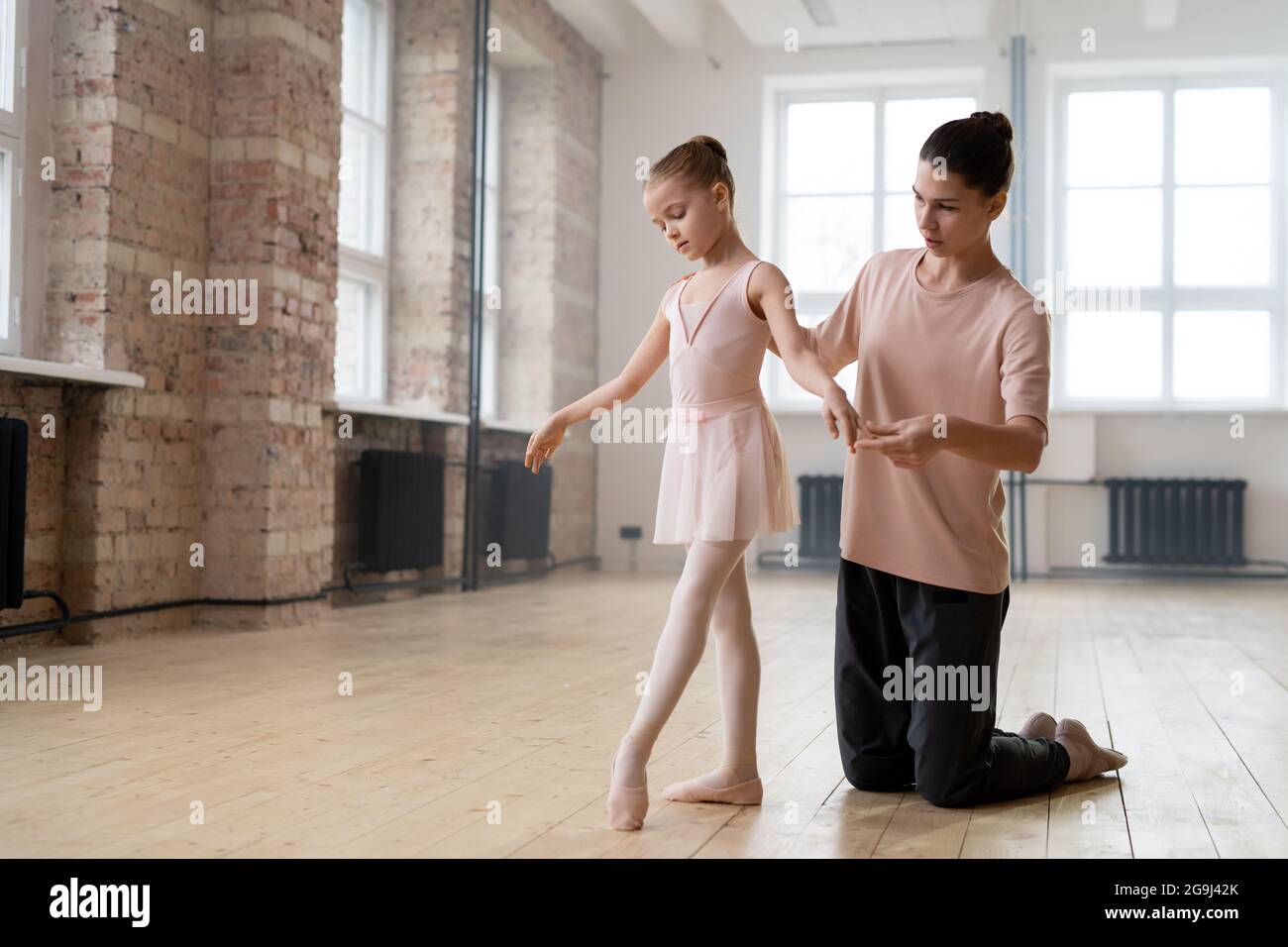 Little girl learning to dance ballet with the help of her trainer in ...