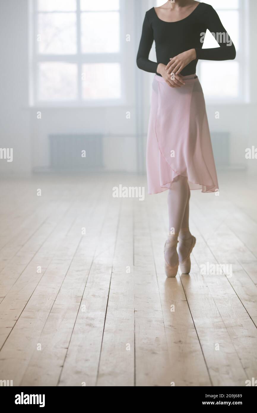 Close-up of woman in tutu dress and in pointe shoes standing on one leg ...