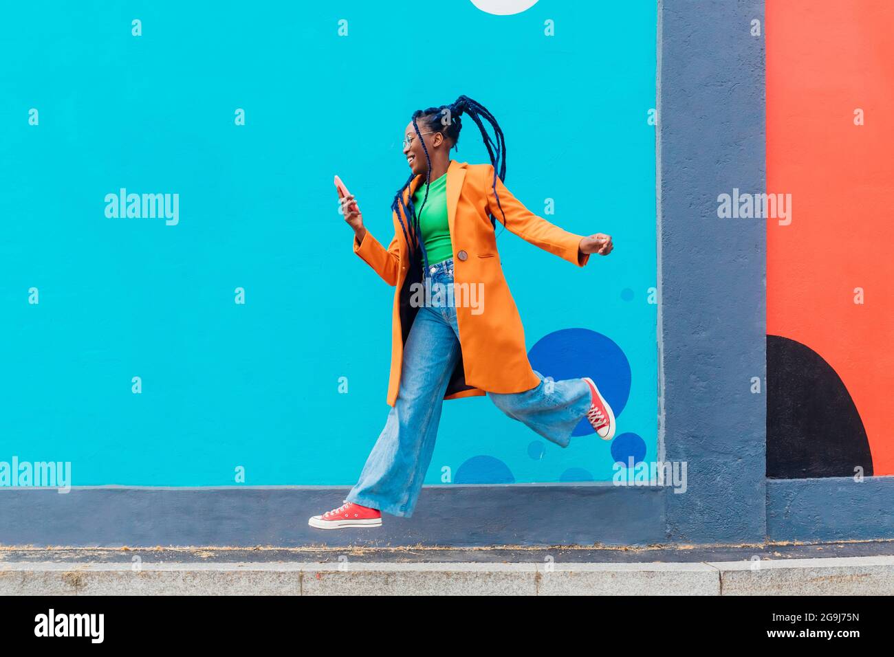 Italy, Milan, Woman with braids jumping against blue wall Stock Photo ...