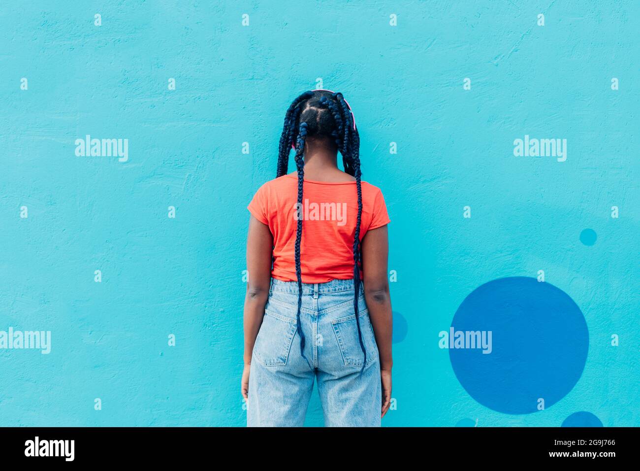 Italy, Milan, Rear view of woman with braids in front of blue wall ...