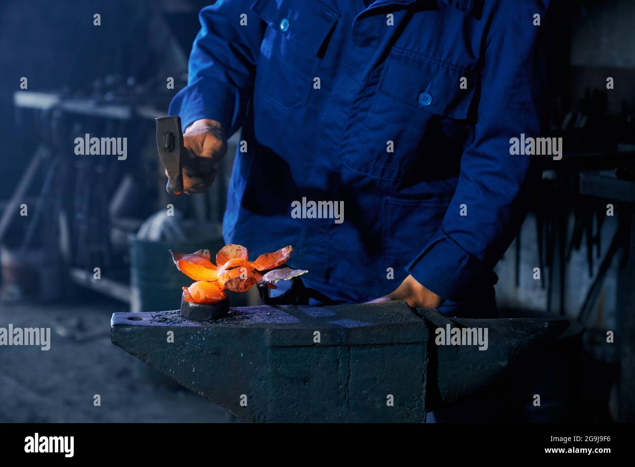 Professional blacksmith in uniform using heavy hammer for forging ...