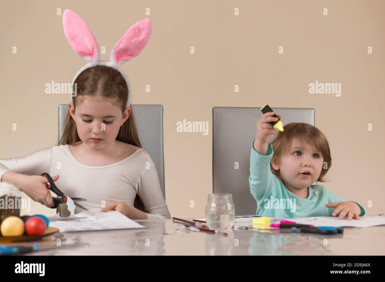 Two sisters at the table draw with markers and cut out crafts from ...
