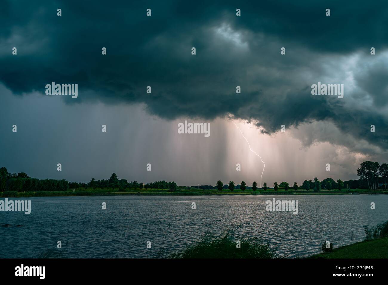Lightning strikes from the base of a thunderstorm over a lake Stock ...