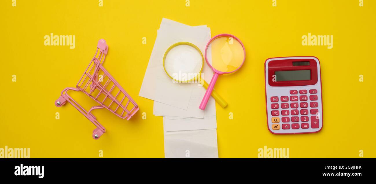 stack of paper checks, a pink plastic calculator and a magnifying glass ...