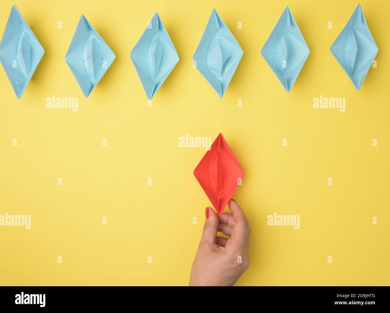 a group of blue paper boats follows a red boat in front of a yellow ...