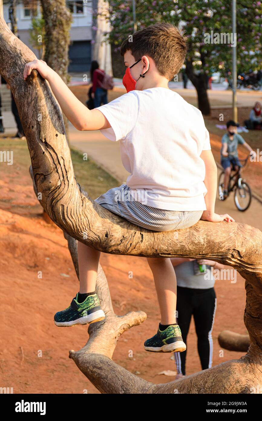 8 year old child, with mask, sitting on a tree trunk in a public square ...