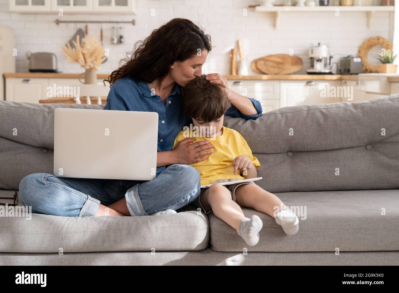 Remote worker mom or freelancer embrace kid with tablet using laptop ...
