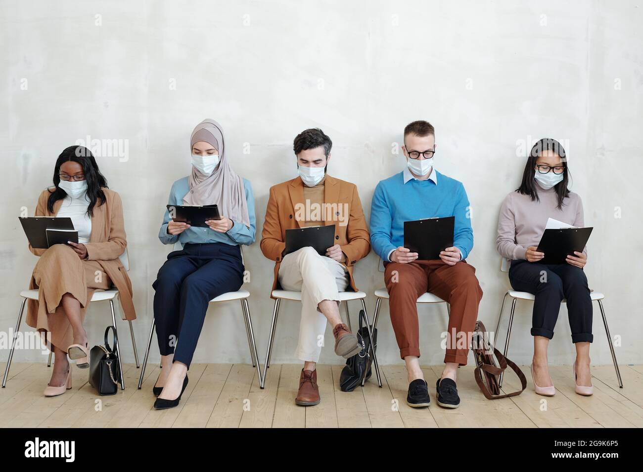 Young multiracial applicants in protective masks looking through their ...