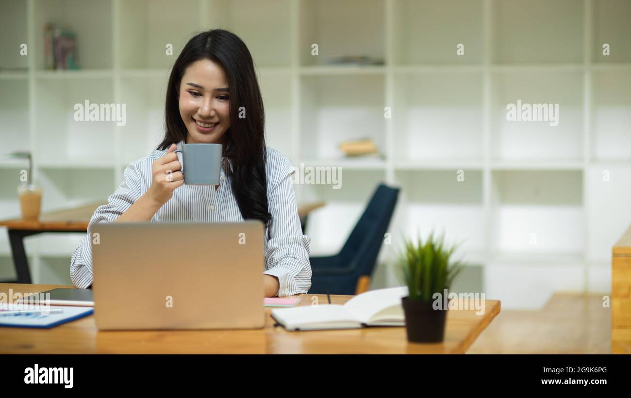 Beautiful marketing officer drinking coffee during working on laptop ...