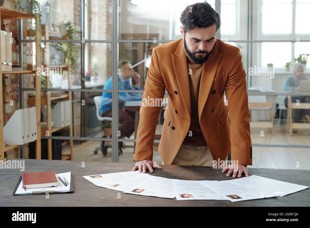 Serious hr manager bending over table while looking through resume of ...