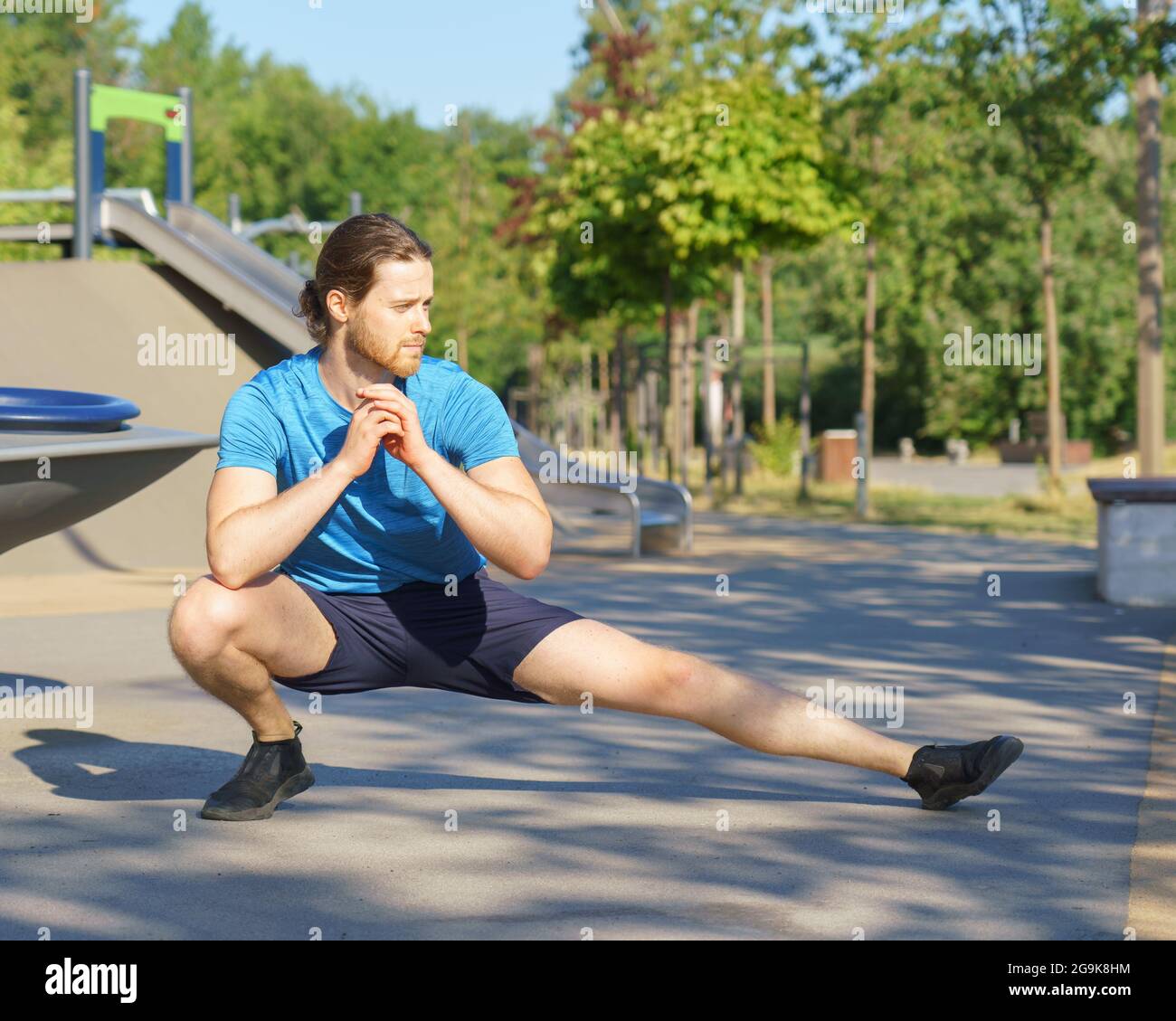 Young fit european man in activewear stretching legs while warming up ...
