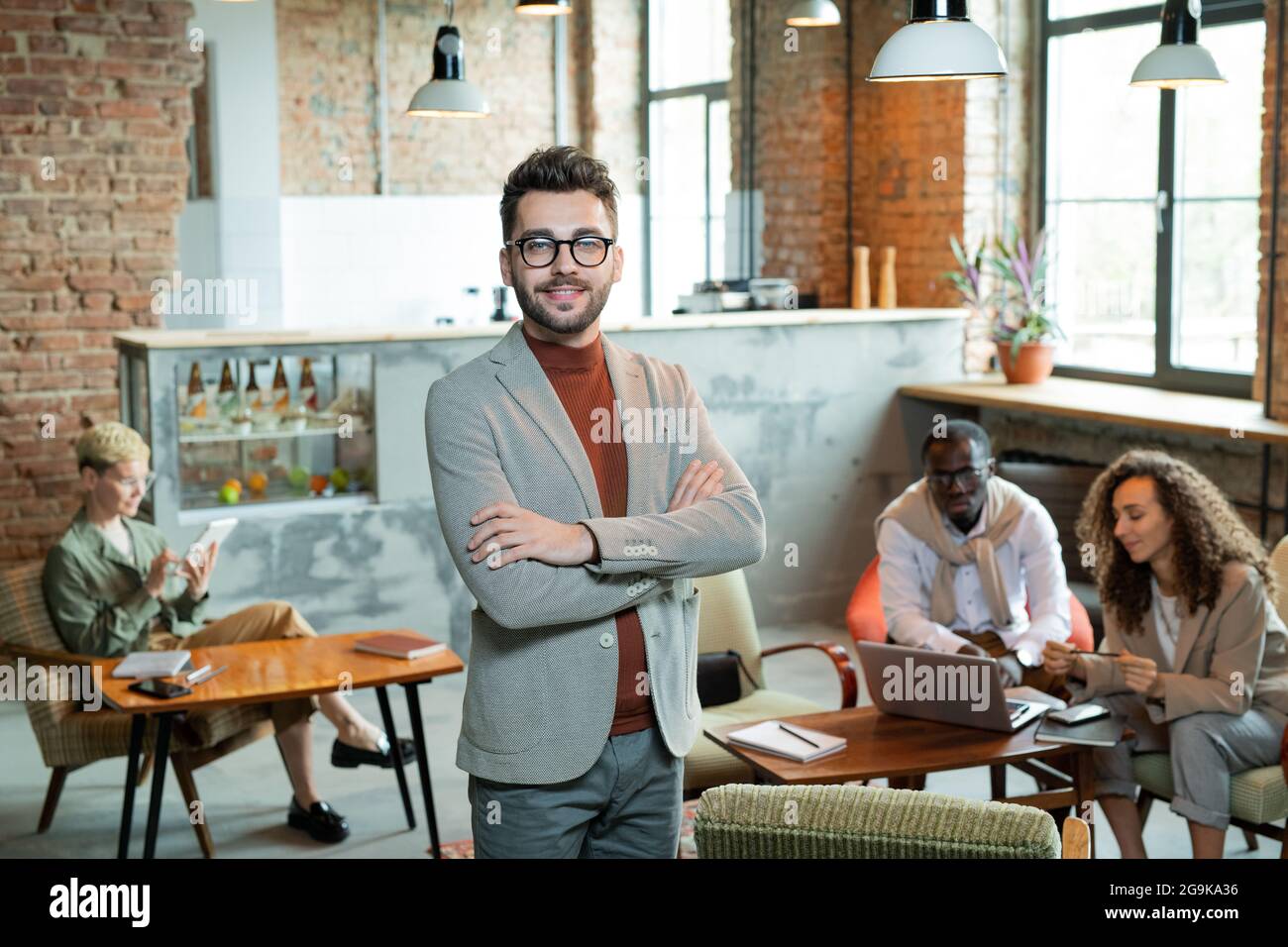 Young smiling cross-armed businessman standing in front of working ...