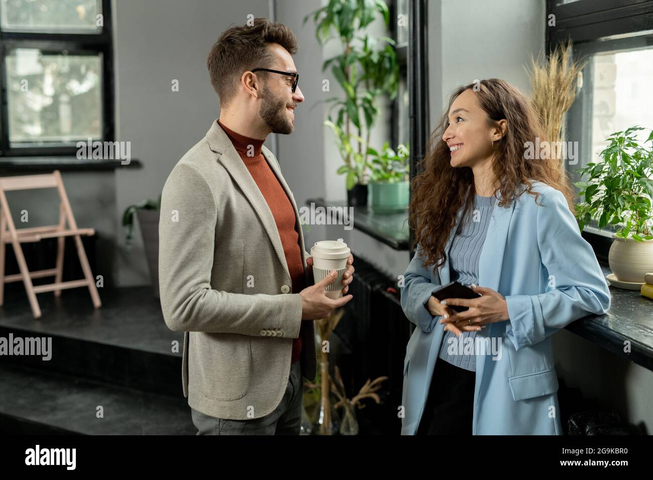 Two young smiling colleagues having discussion at break in office Stock ...