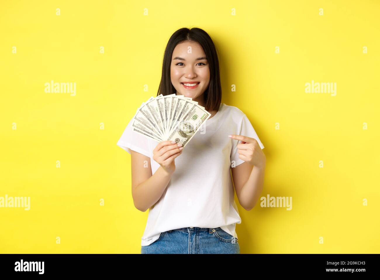 Young asian woman smiling, showing prize money, pointing finger at ...