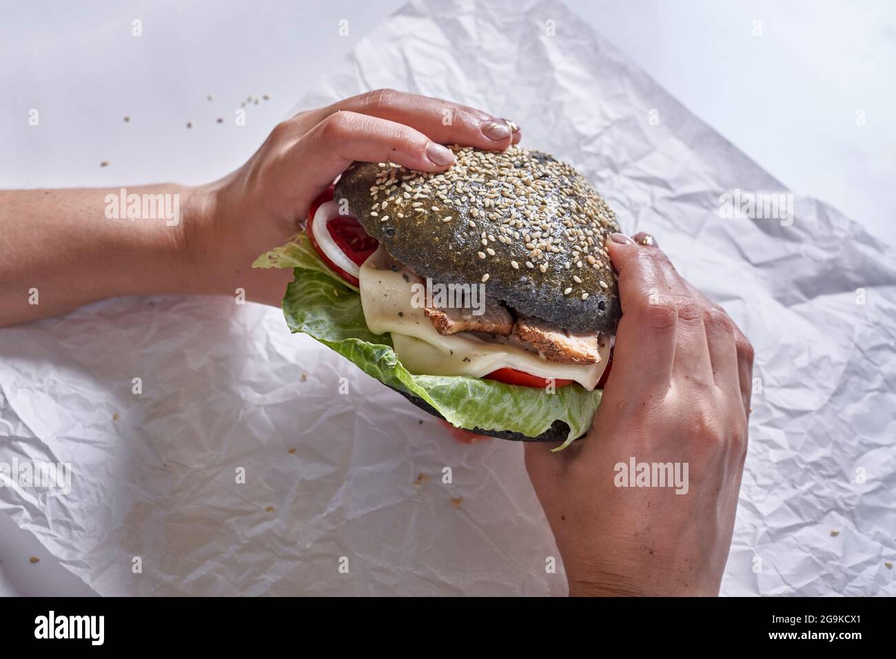 Eating black burger. Cropped shot of a person eating trendy black ...