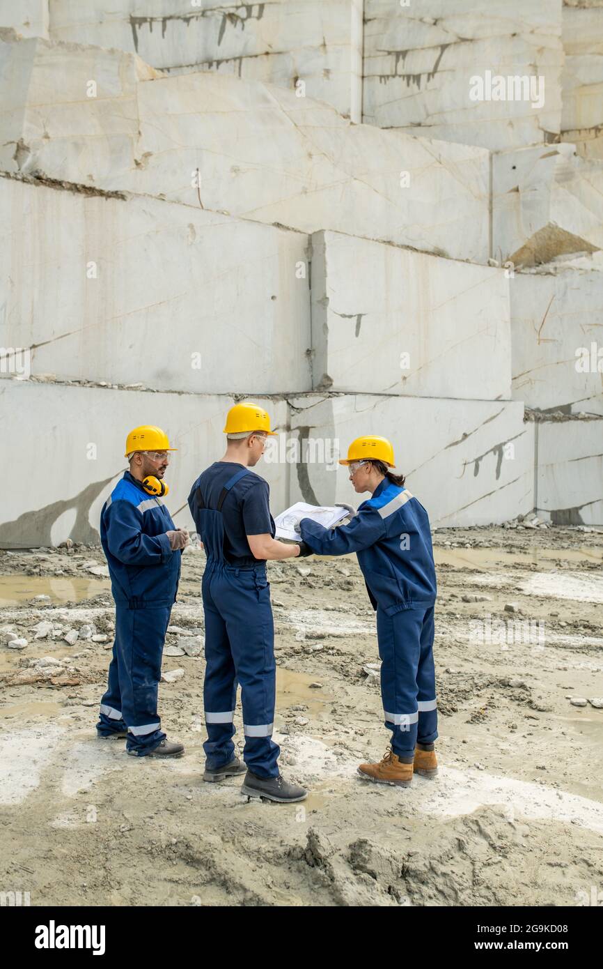 Group of builders discussing blueprint by block wall at building place ...