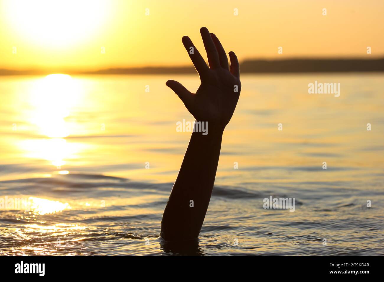 A man is drowning in water on a sunset. A hand peeks out from under a ...