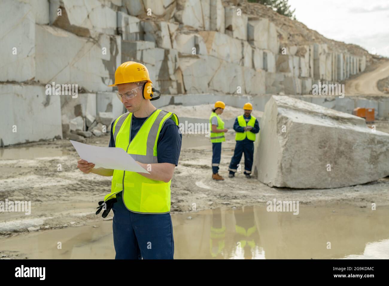 Serious builder looking at blueprint against his two colleagues at ...