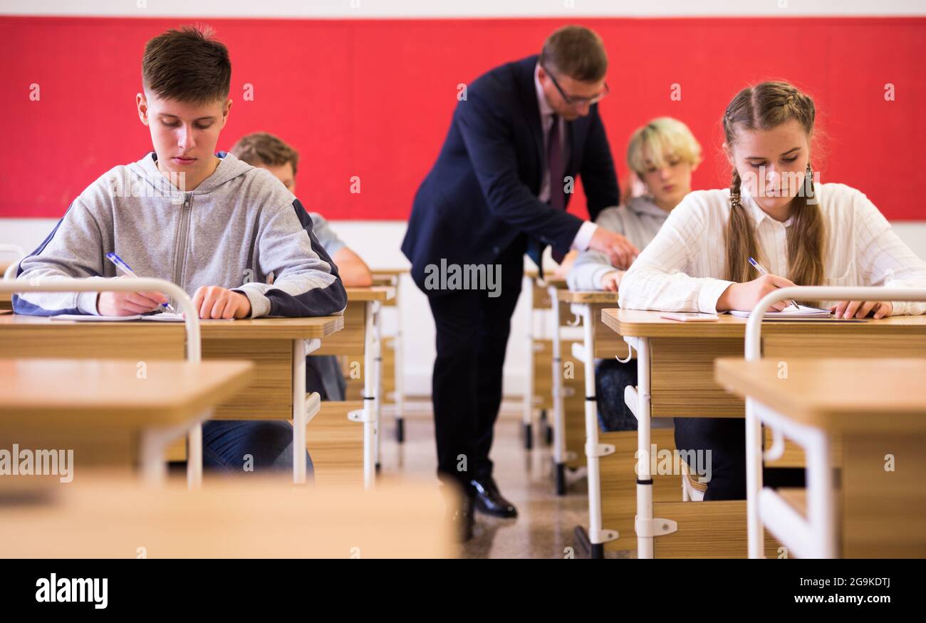 Teenagers listening to lecturer and writing in notebooks in classroom ...