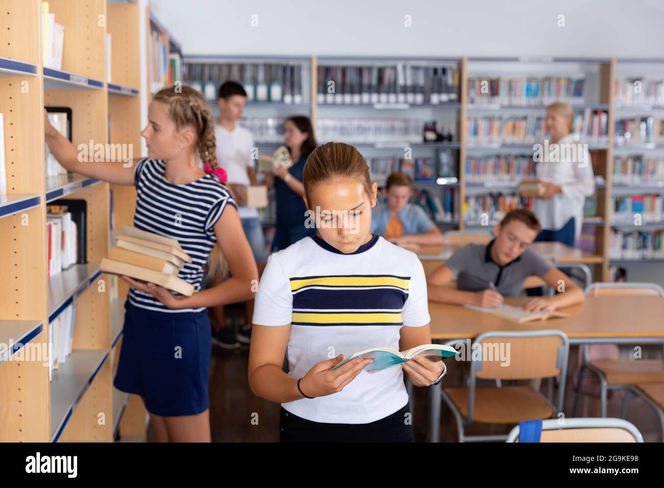 Schoolgirl standing with book before lesson in school library, reading ...