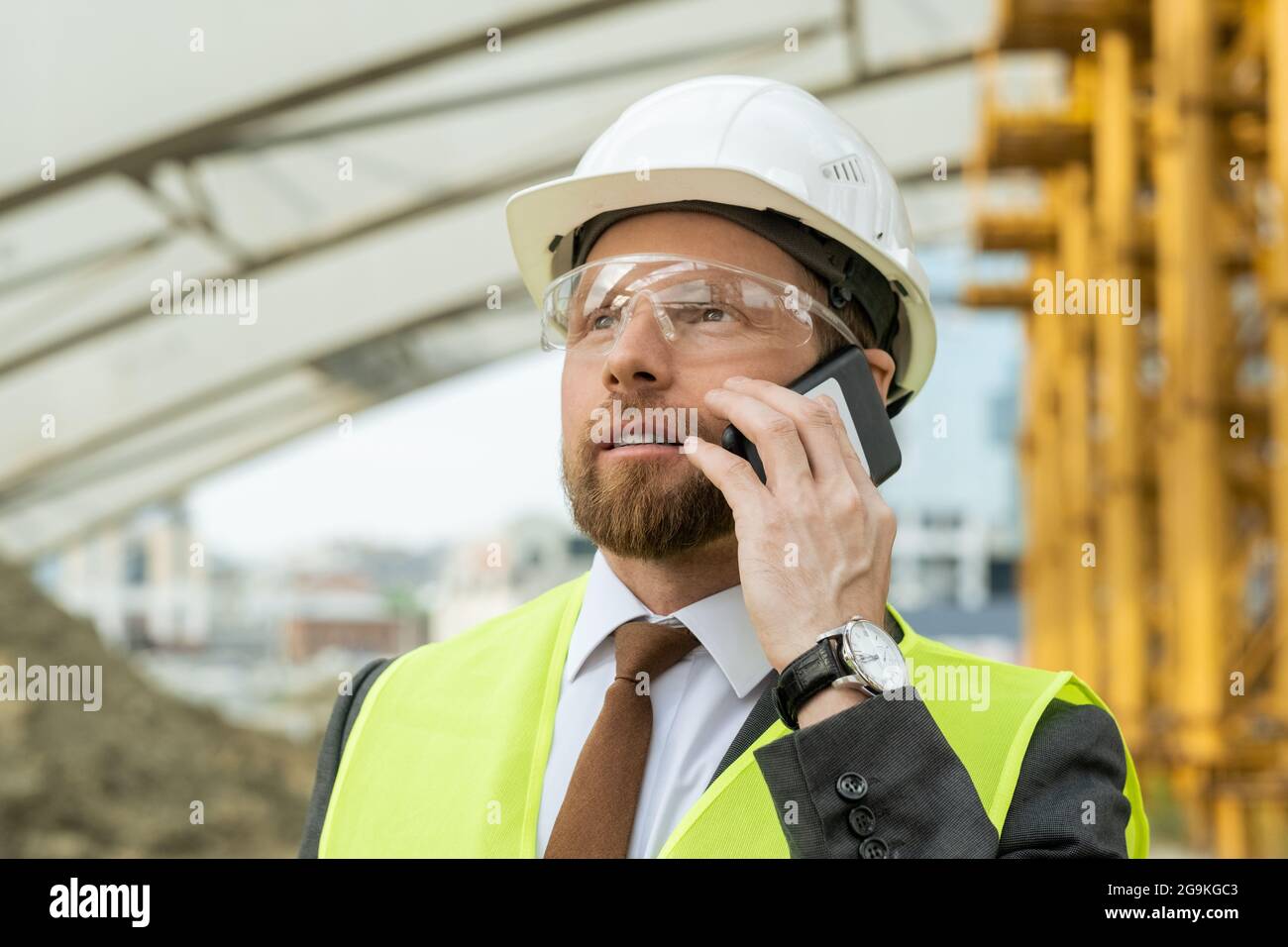 Young engineer in work helmet talking on mobile phone while working on ...