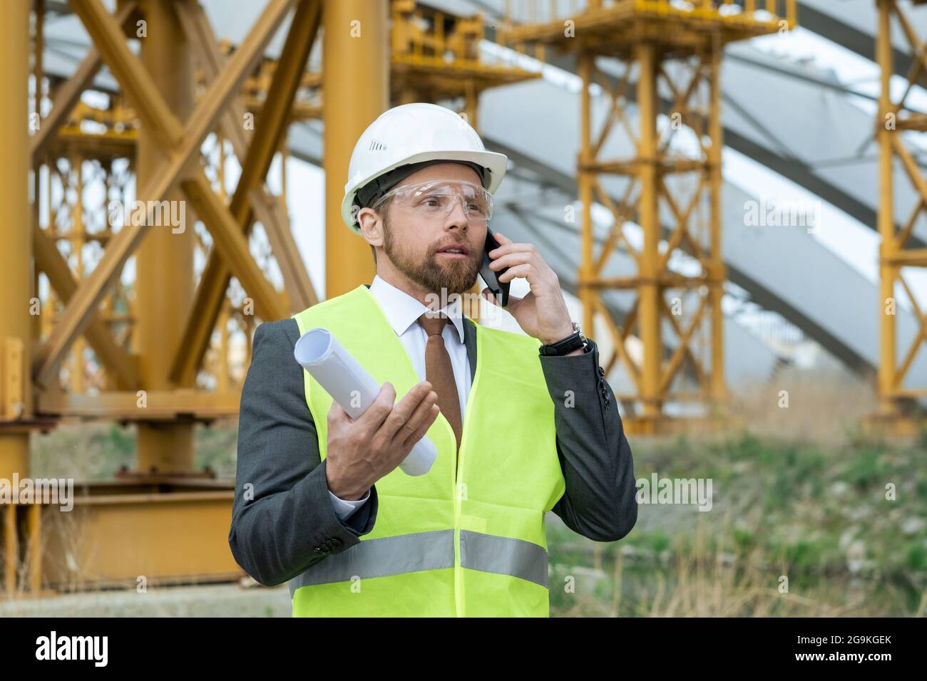 Young architect in work helmet discussing new project on mobile phone ...