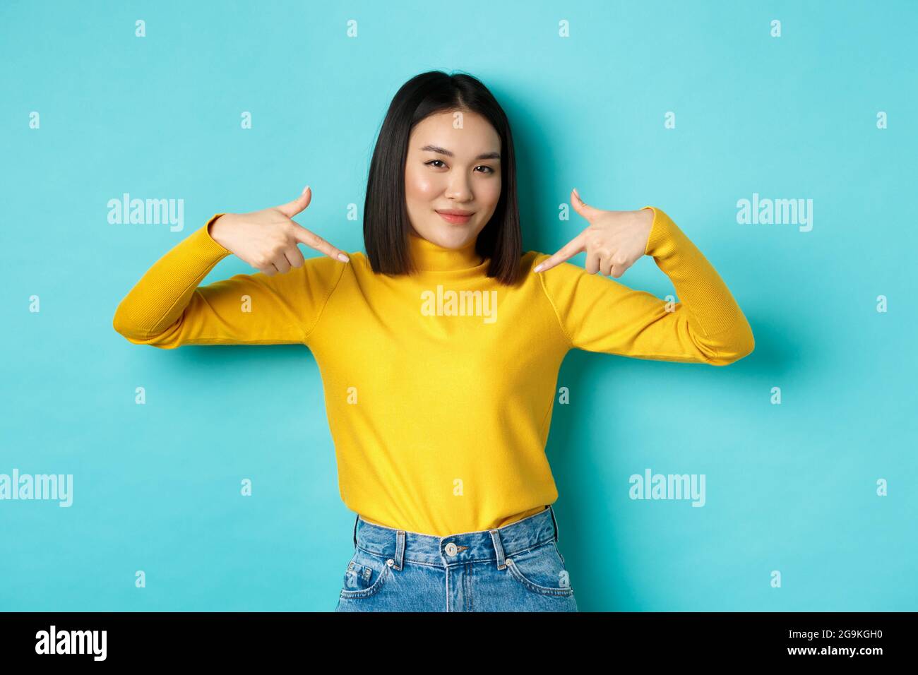 Confident asian woman in stylish sweater pointing fingers at logo on ...