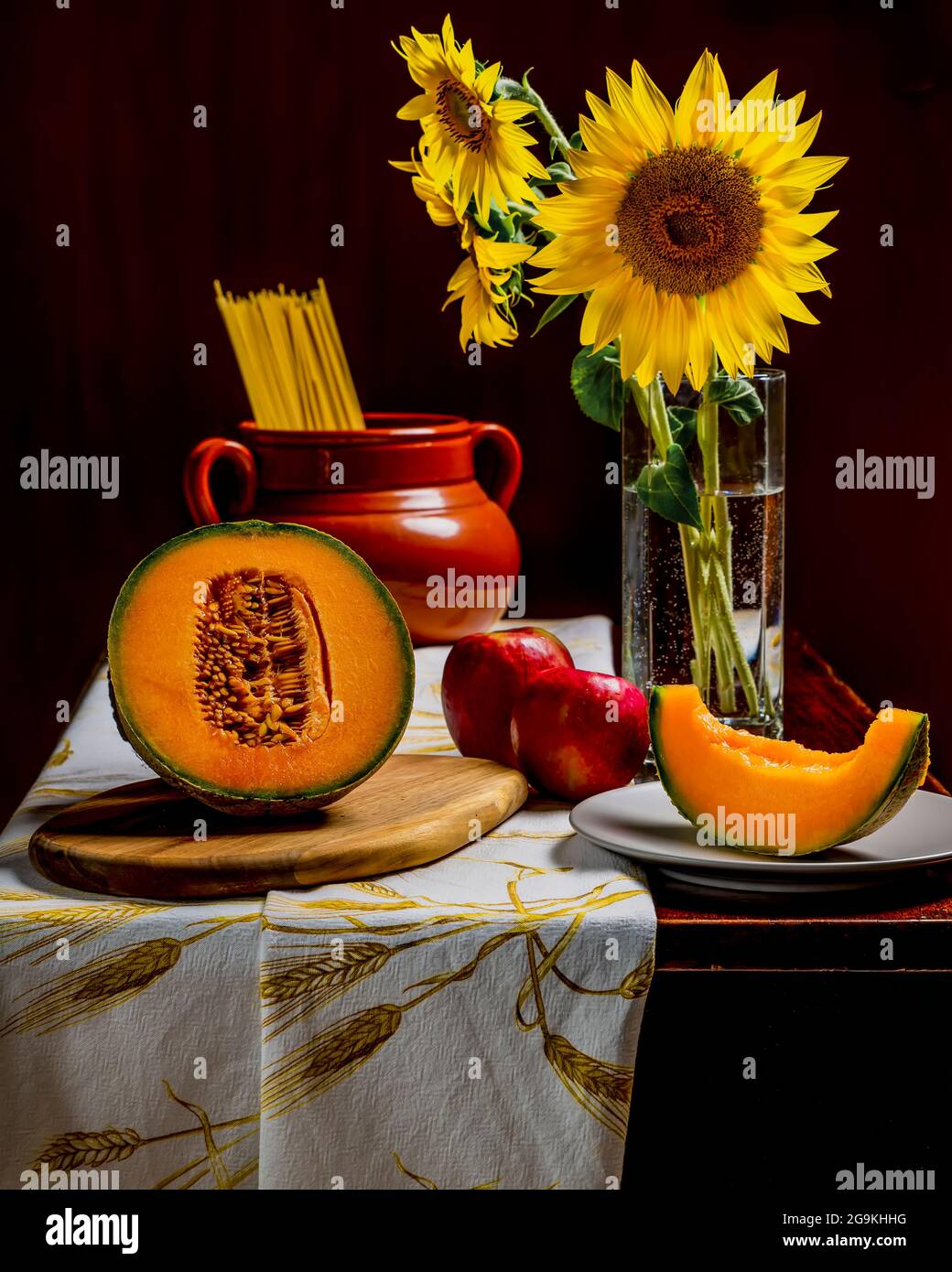 A melon in half and a slice on a plate with two red apples, sunflowers ...