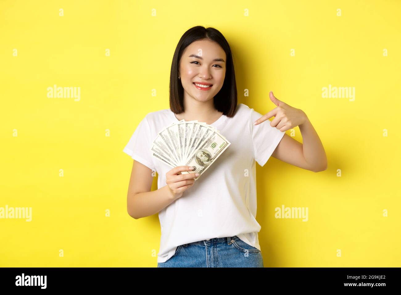 Young asian woman smiling, showing prize money, pointing finger at ...