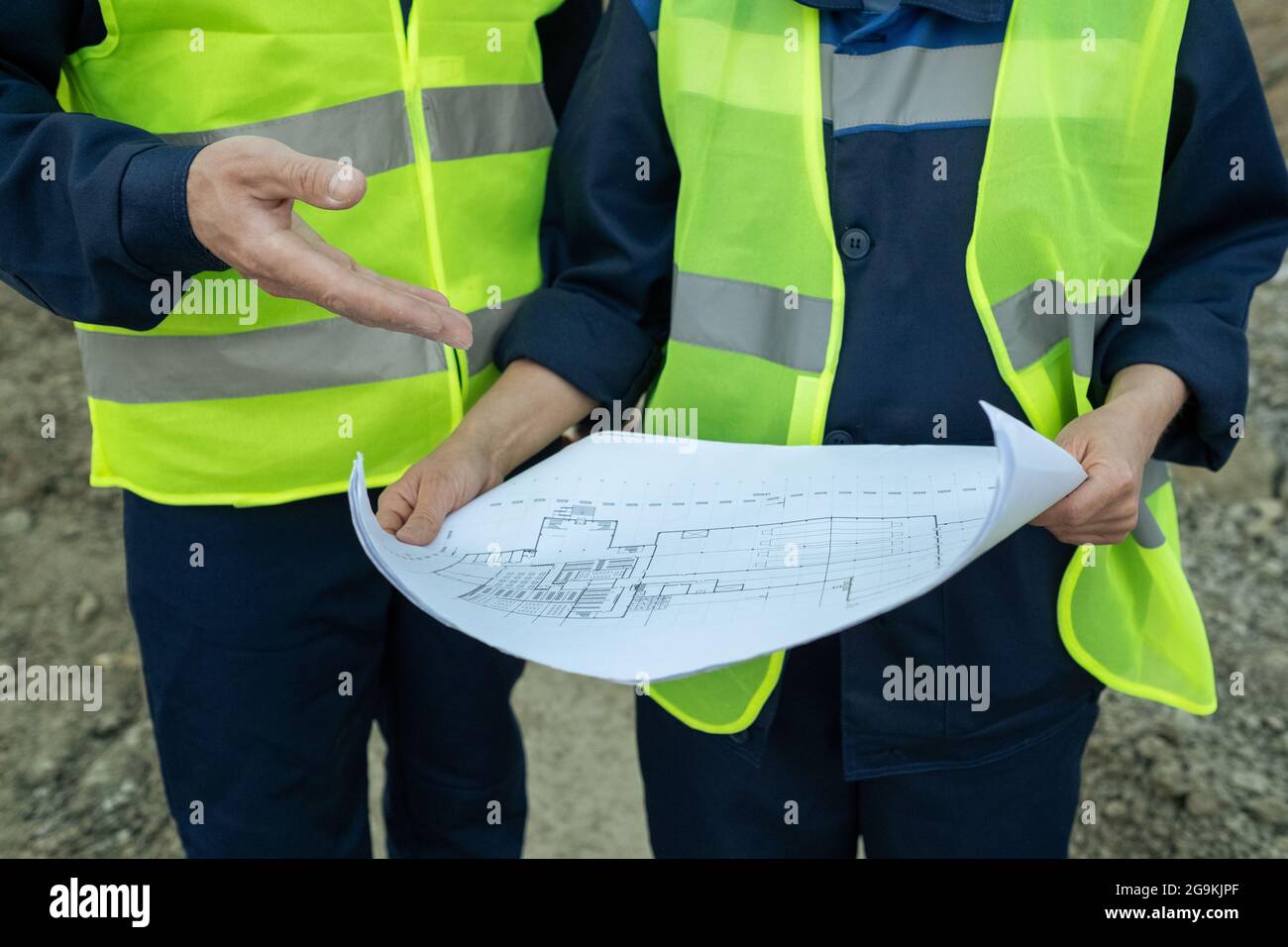 Close-up of two engineers in reflective clothing examining blueprint of ...