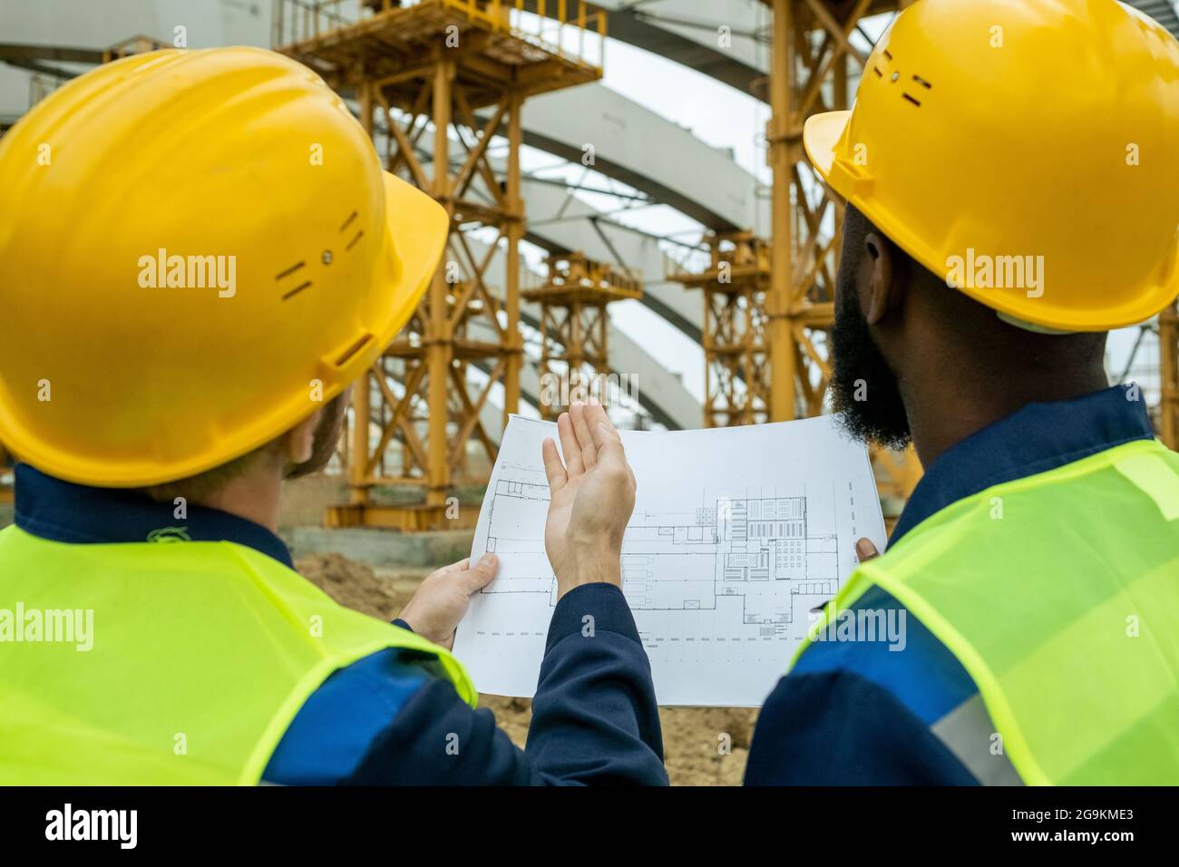 Rear view of two construction workers working at construction site hi ...