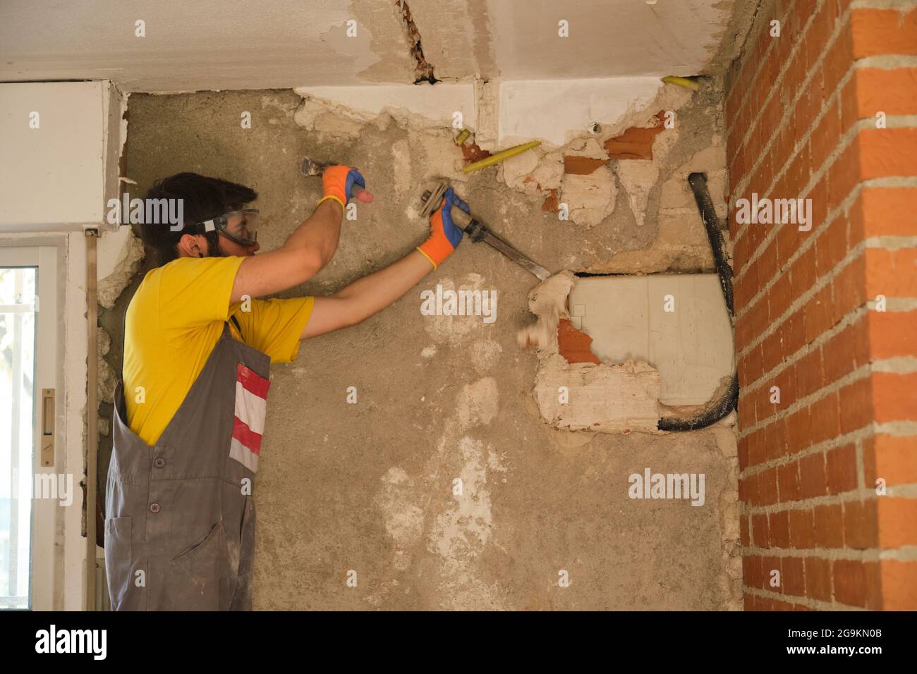 Young caucasian construction worker breaking up a house wall with a ...
