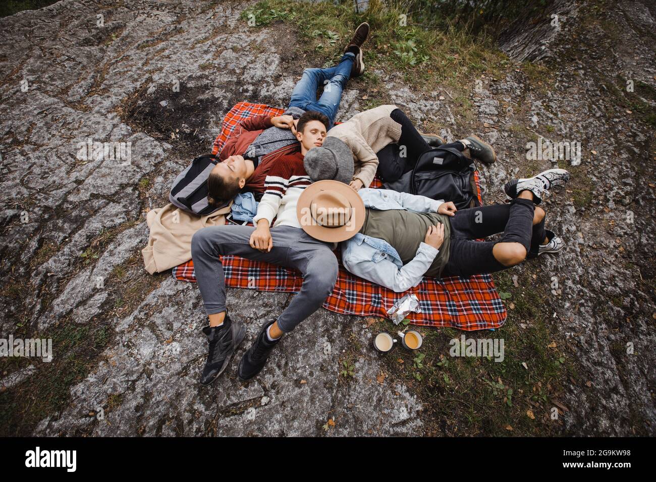From above of group of male travelers lying on plaid on rocky ground ...