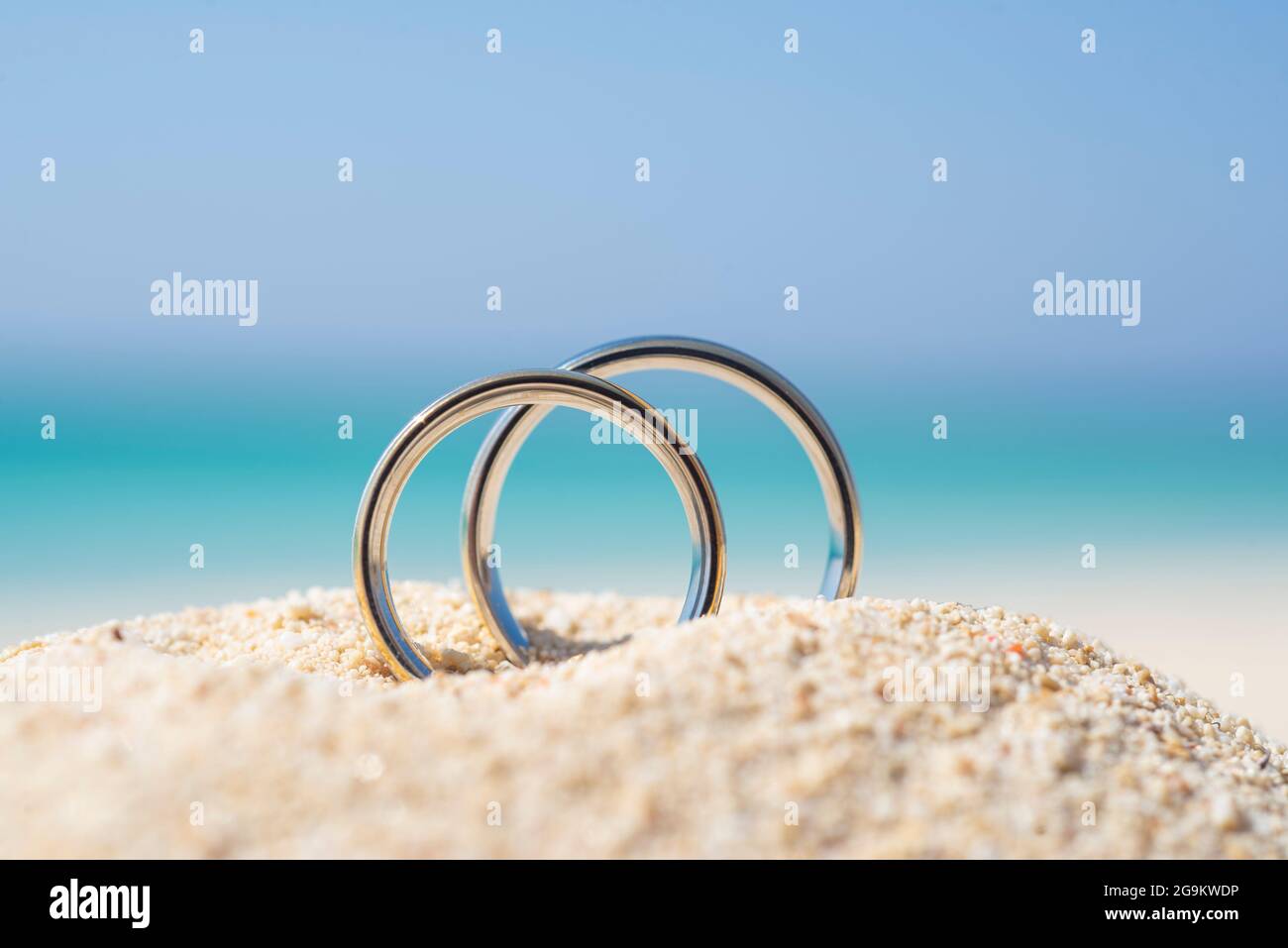 Pair of white gold wedding ring bands jewelry in sand on tropical ...