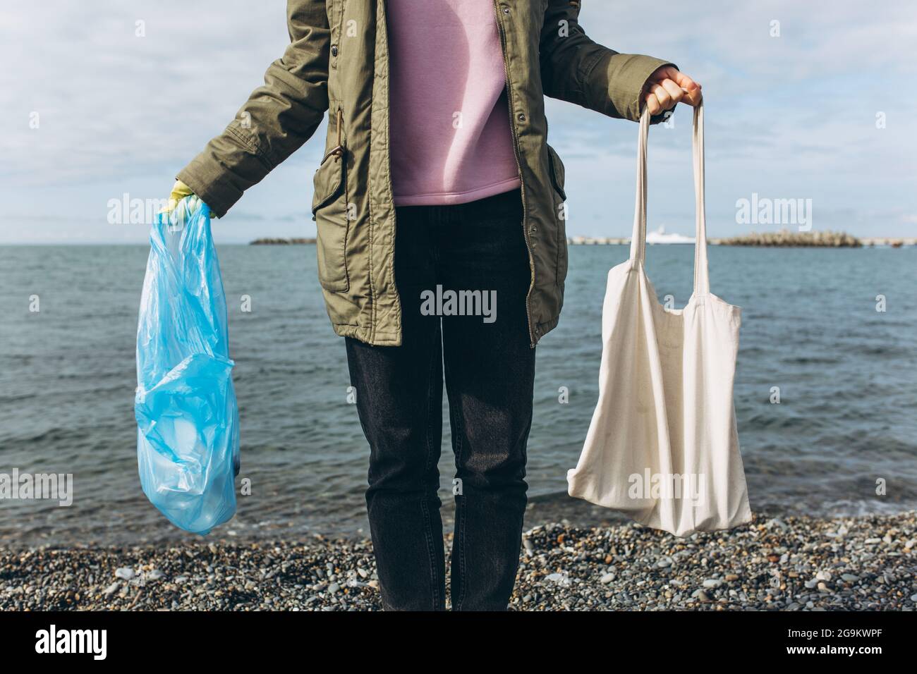 A female volunteer holds a garbage bag and a reusable canvas bag in her ...