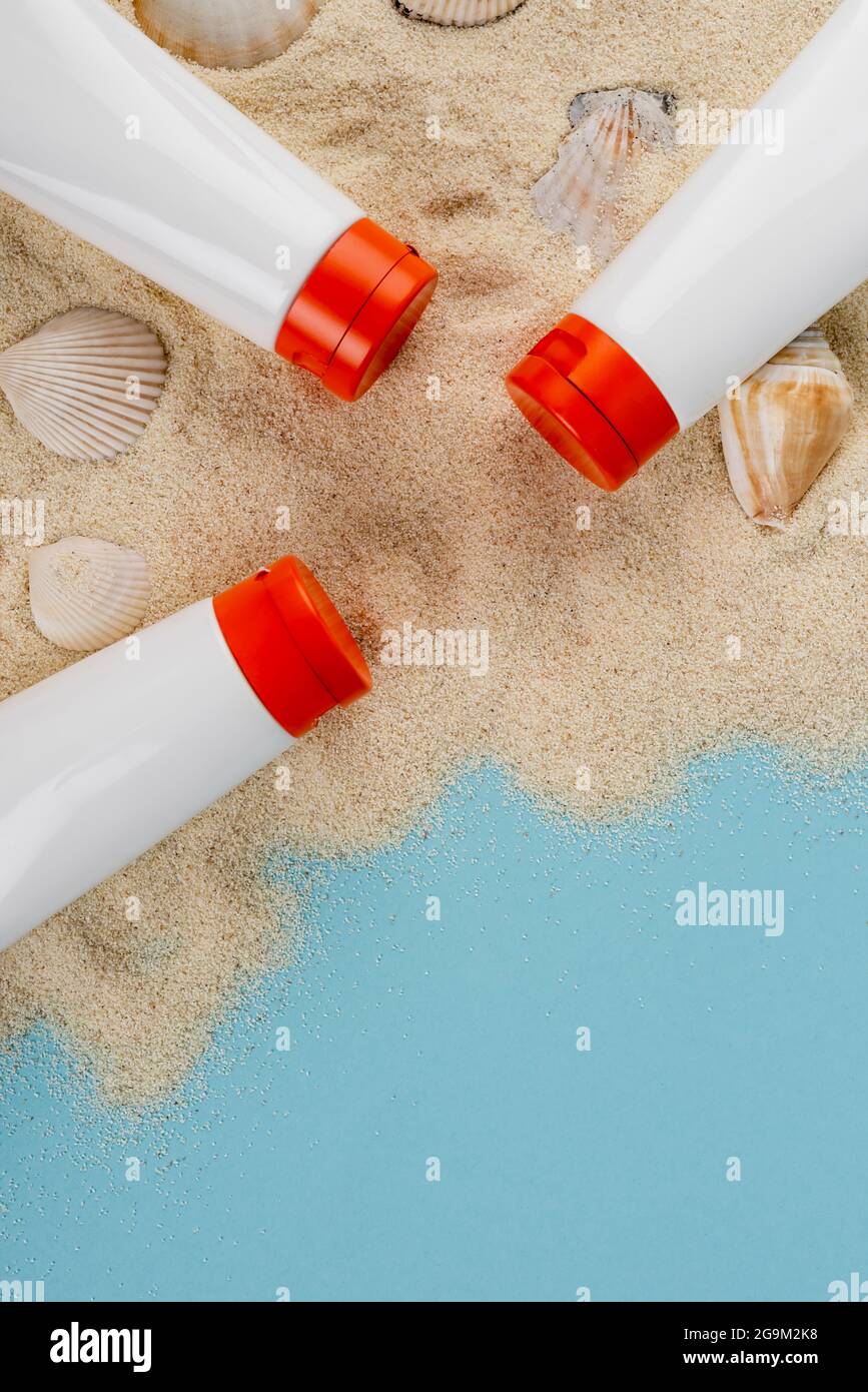 top view of seashells and tubes with sunblock on sand and blue surface ...