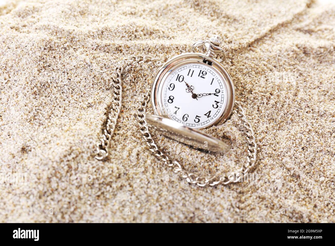 Silver pocket clock on sand background Stock Photo - Alamy