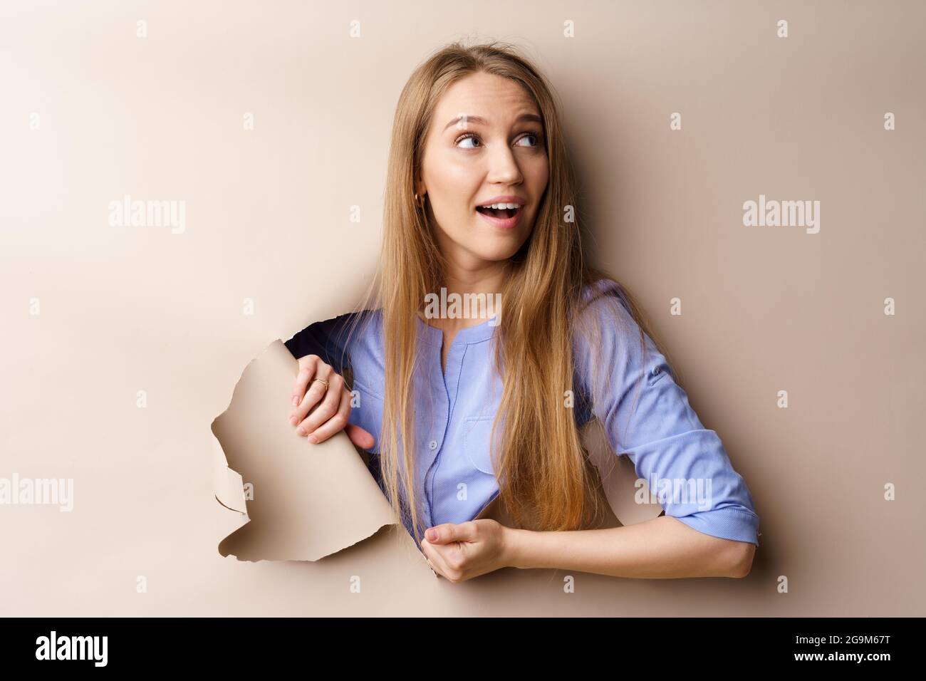 Beautiful young woman looking through a hole in beige paper Stock Photo ...