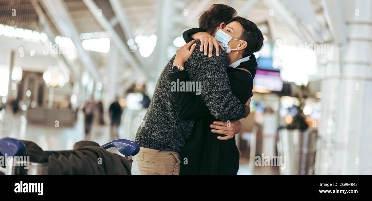 Husband and wife embracing each other at airport. Female wearing face ...