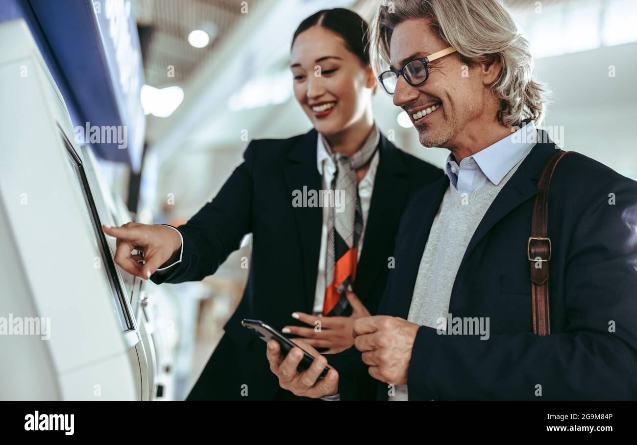 Flight attendant assisting male traveler in doing the self check-in ...