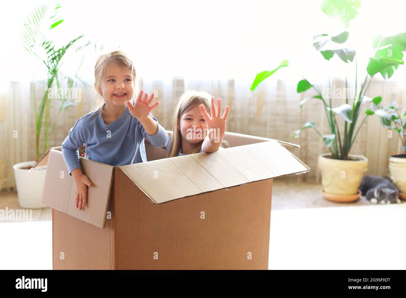 Big carton box with cheerful girls waving hands while playing at home ...